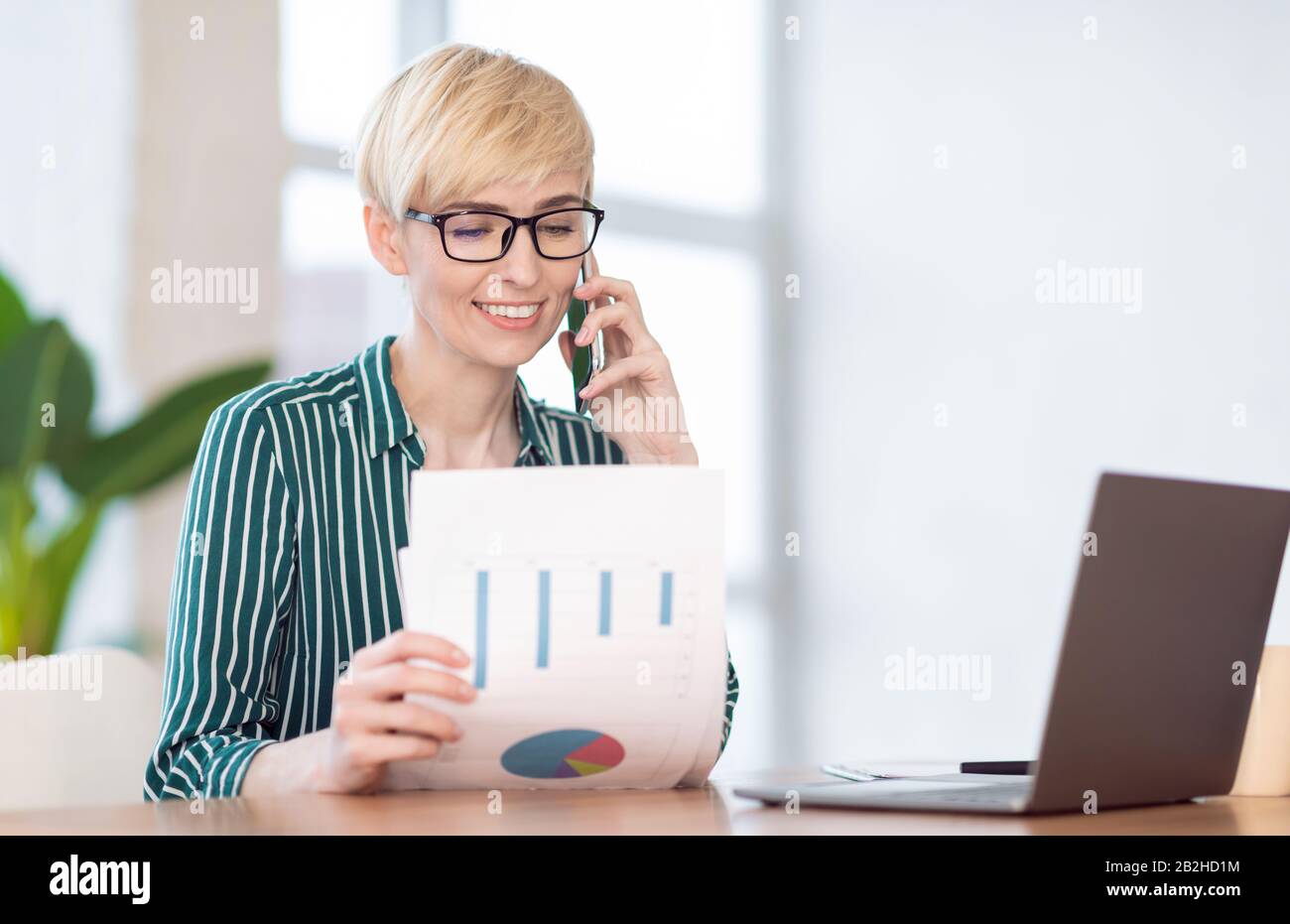 Happy Businesswoman Talking On Phone Holding Charts Sitting In Office ...