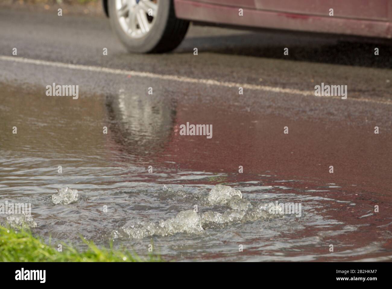 Traffic passing water flooding out of a manhole cover near Gillingham ...