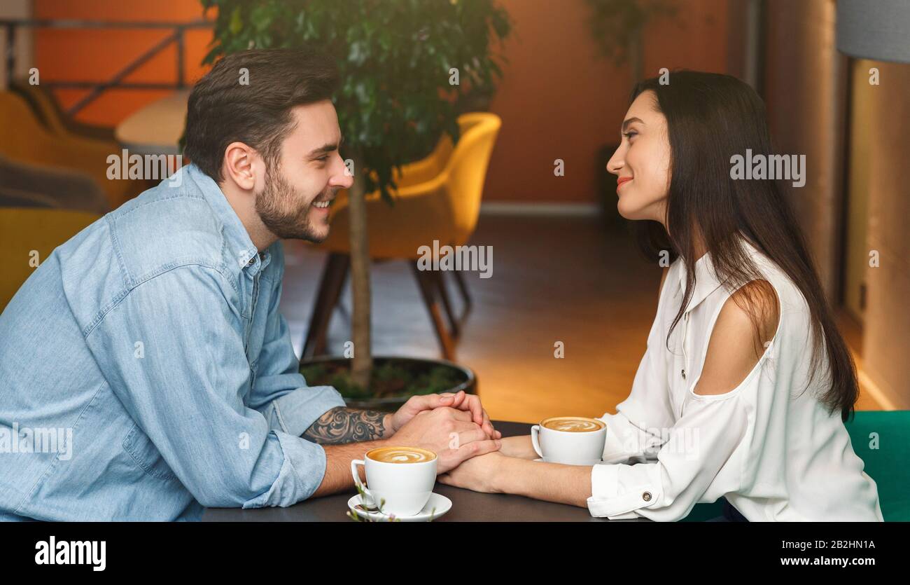 Boyfriend And Girlfriend Holding Hands Flirting In Cafe, Side View ...