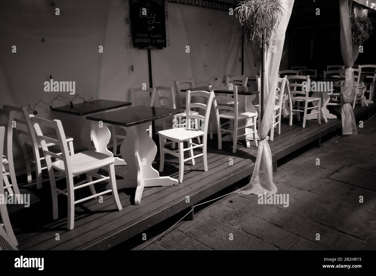 White chairs and tables on a wooden deck on the street, a Trattoria ...