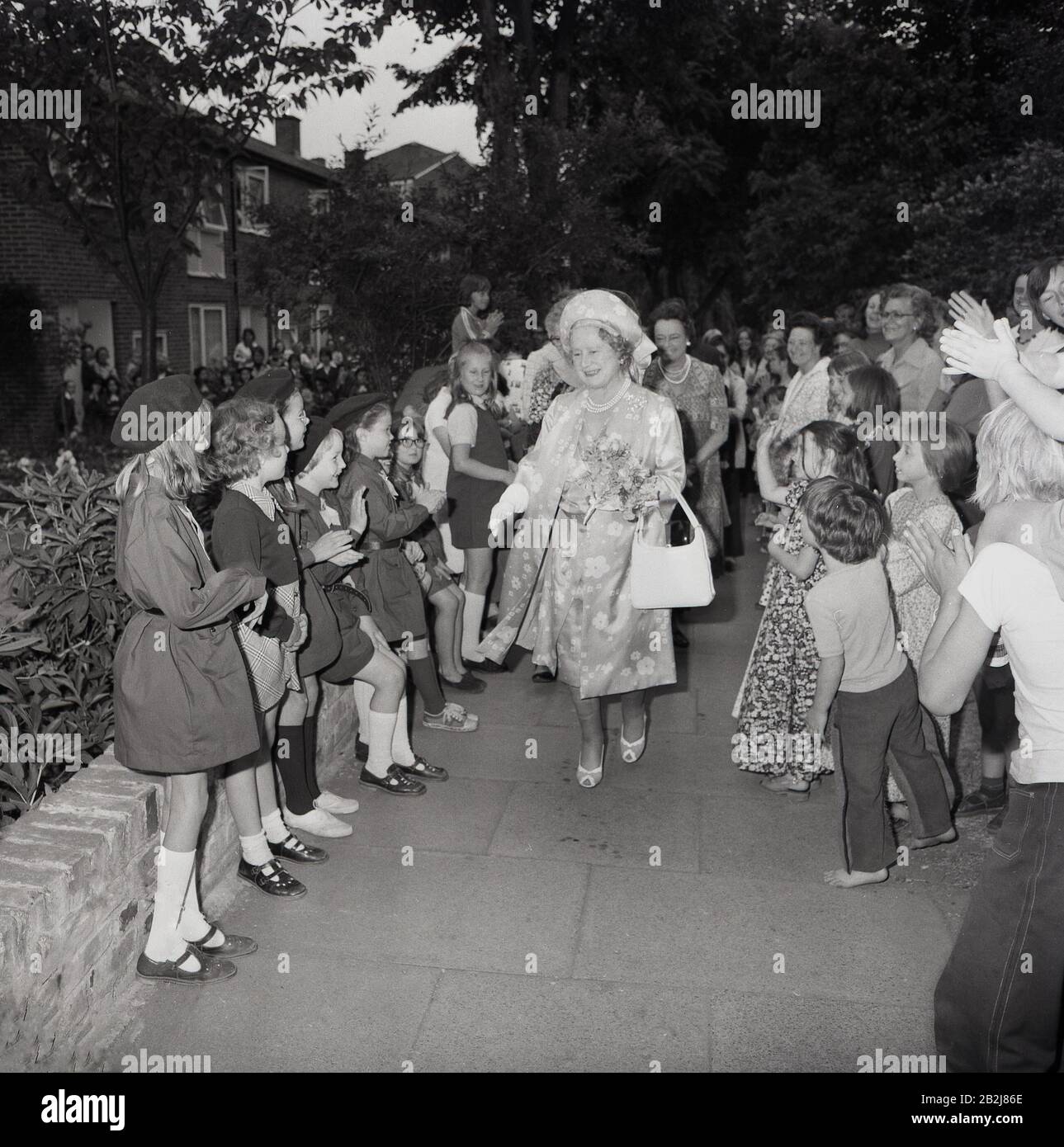 1970s, historical, excited children and local people line the pavement ...