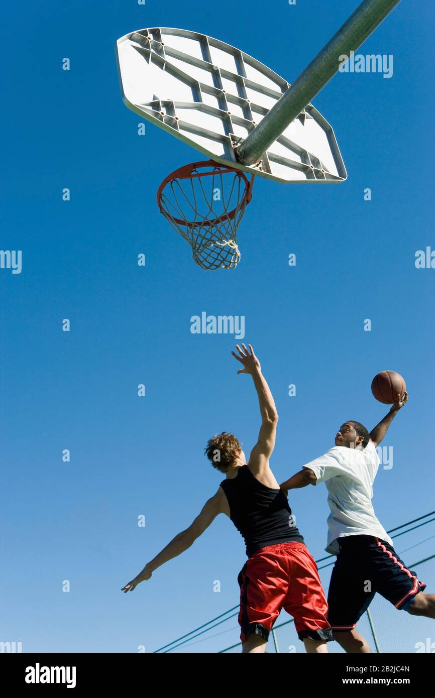 Basketball player guarding another as he tries to shoot basketball low ...