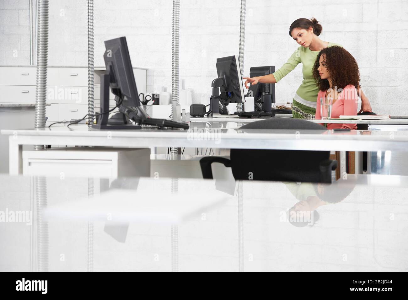 Two young women at desk one pointing at computer monitor Stock Photo ...