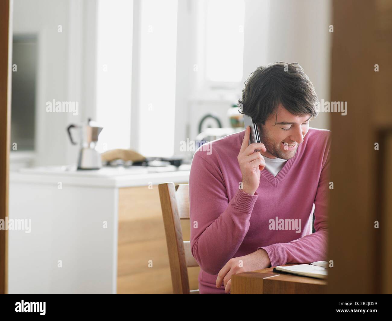 Man sitting in kitchen using phone Stock Photo - Alamy