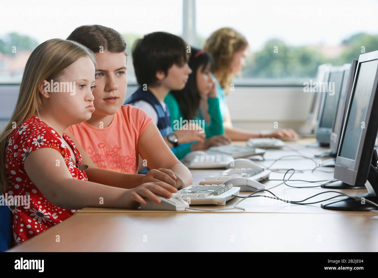 Two girls (10-12) using computer in computer lab children in background ...
