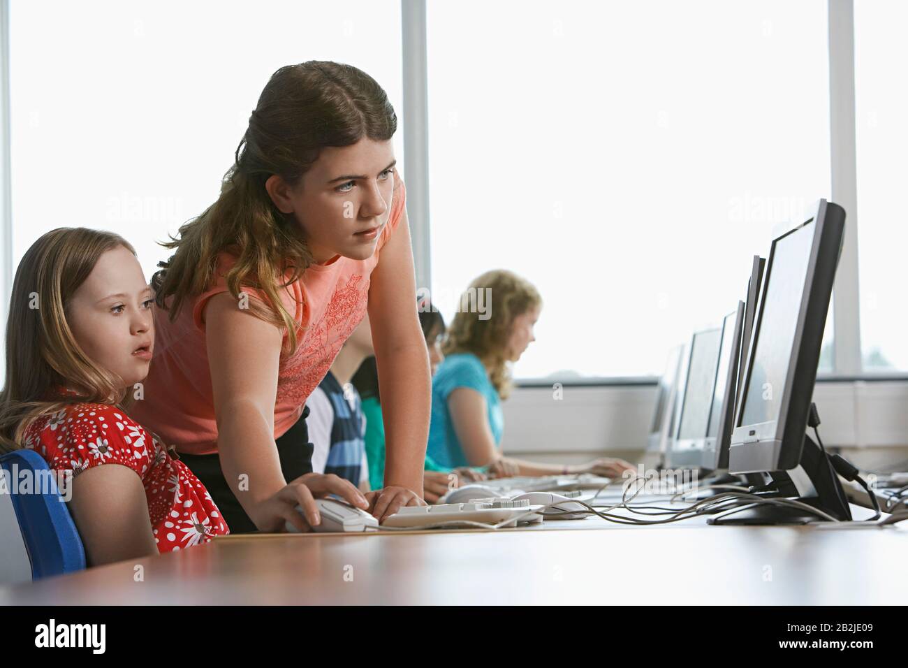 Two girls (10-12) using computer in computer lab children in background ...