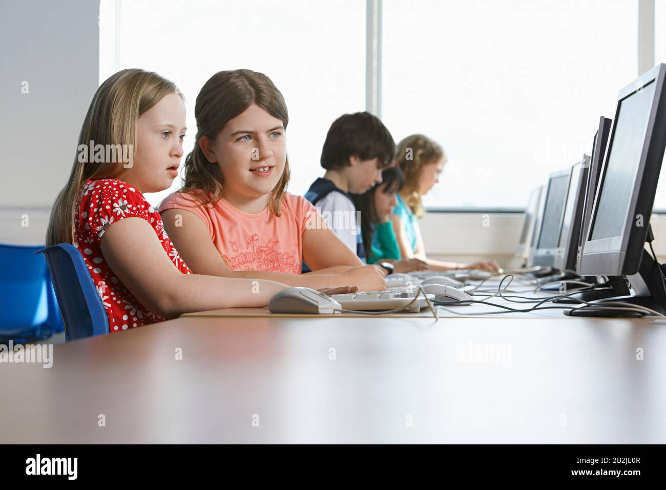 Two girls (10-12) using computer in computer lab children in background ...
