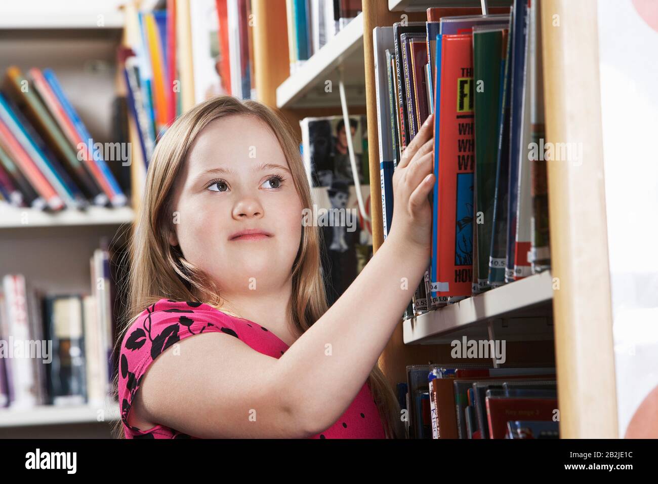 Girl (10-12) with Down syndrome taking book from shelf Stock Photo - Alamy