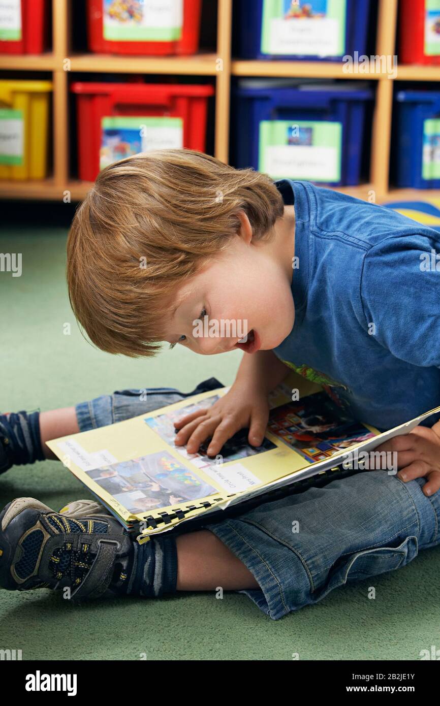 Boy (5-6) with Down syndrome reading book in kindergarten Stock Photo ...