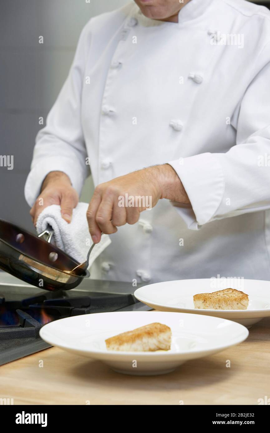 Male chef holding frying pan serving food onto dishes in kitchen Stock ...