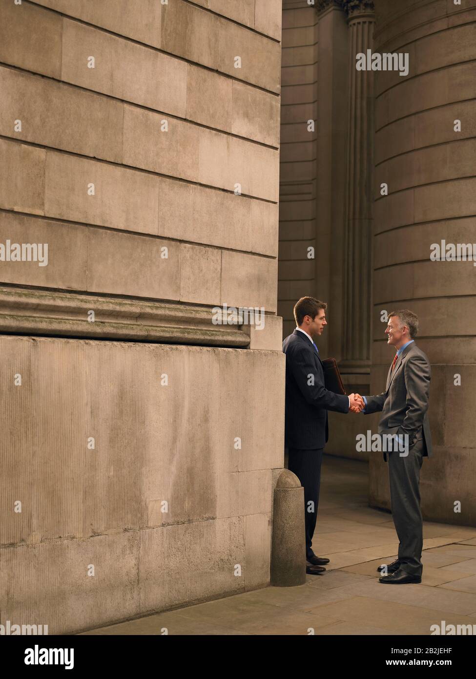 Two businessmen shaking hands at entrance of monumental building Stock ...