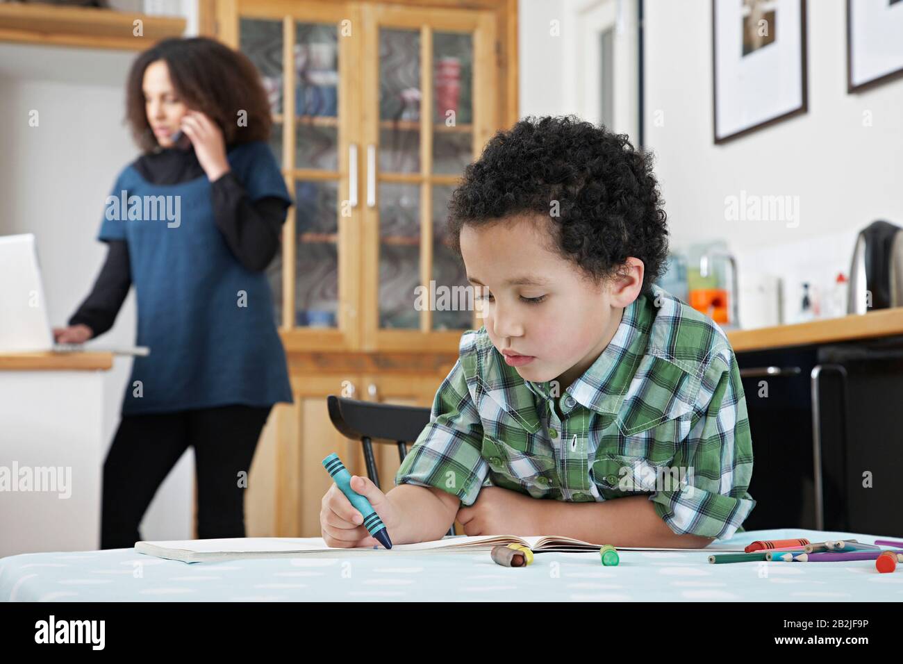 Boy (5-6) colouring with crayon mother on phone in background Stock ...