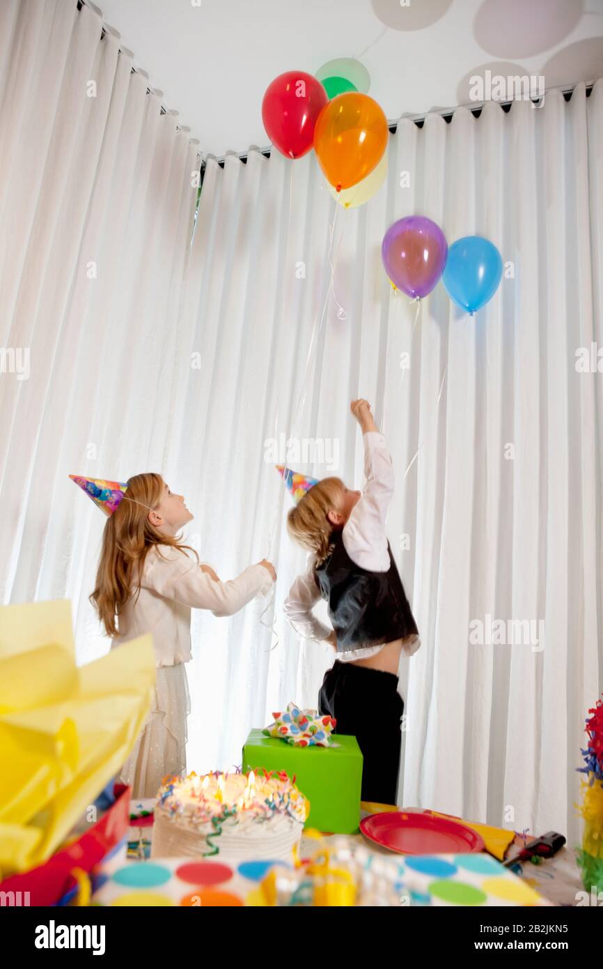 Brother and sister catching helium party balloon Stock Photo - Alamy