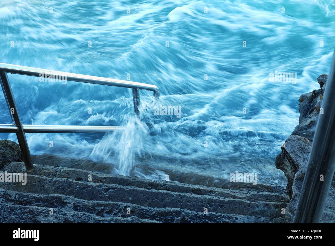 Ocean white water surges, foams and washes around the steps and ...