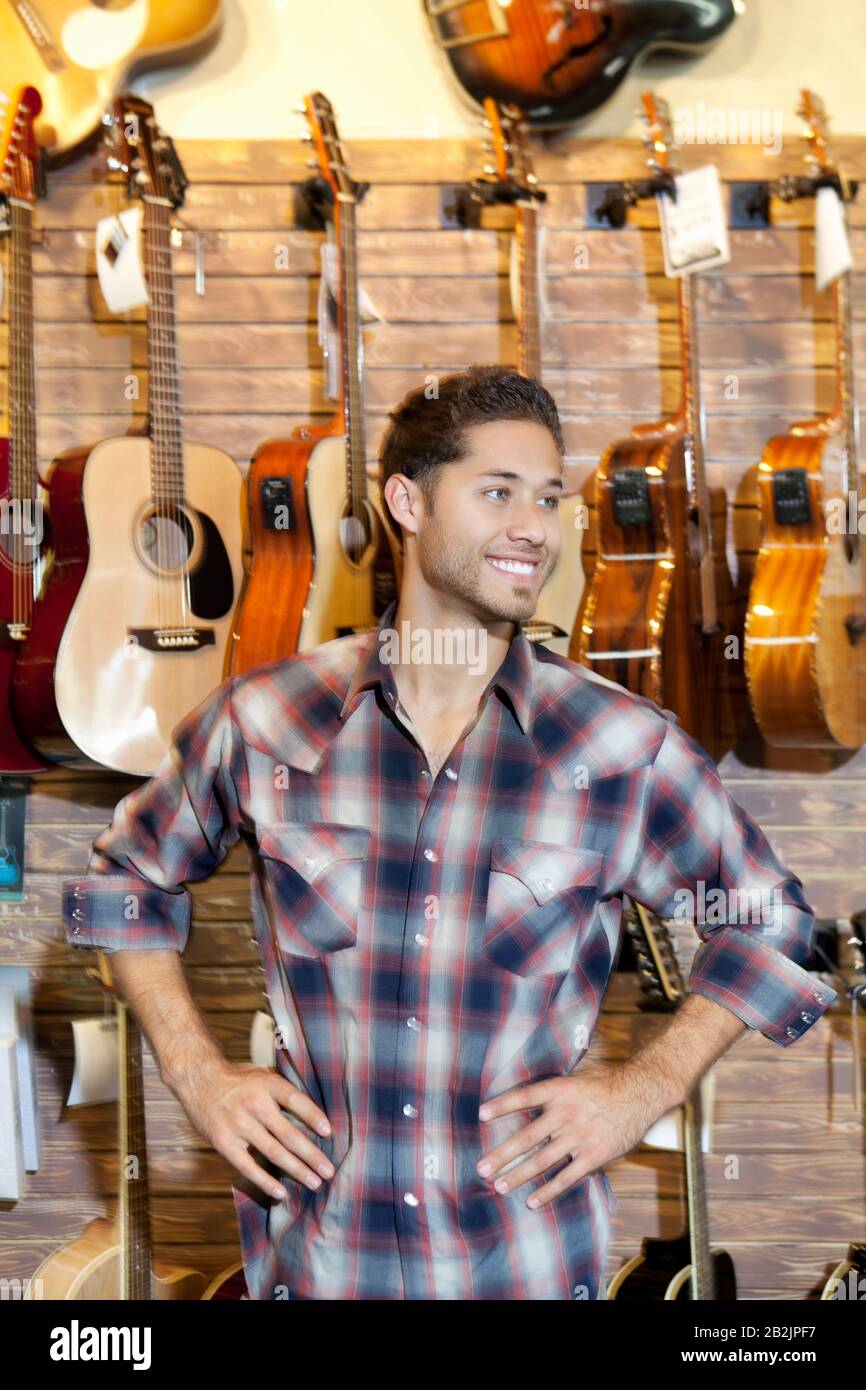 Happy young music store owner with hands on hips standing in front of ...