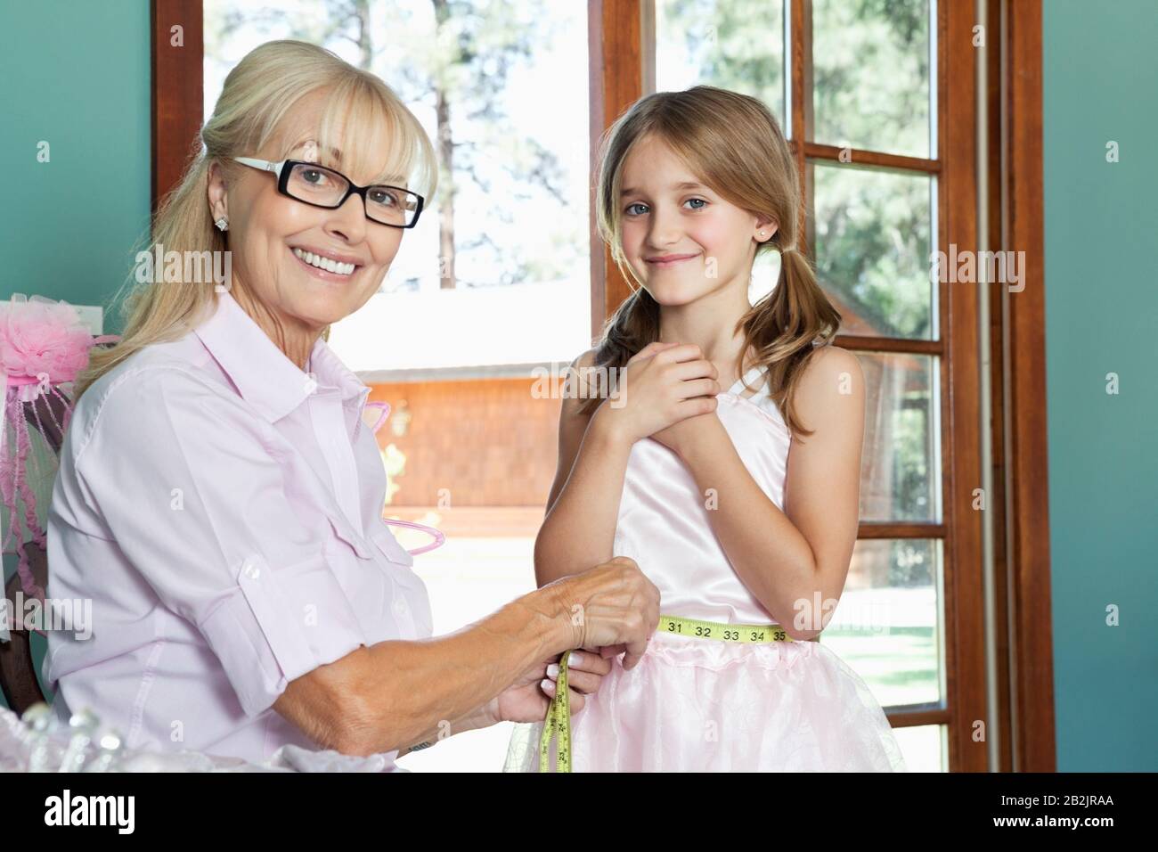 Portrait of grandmother measuring granddaughter's waist with tape Stock ...