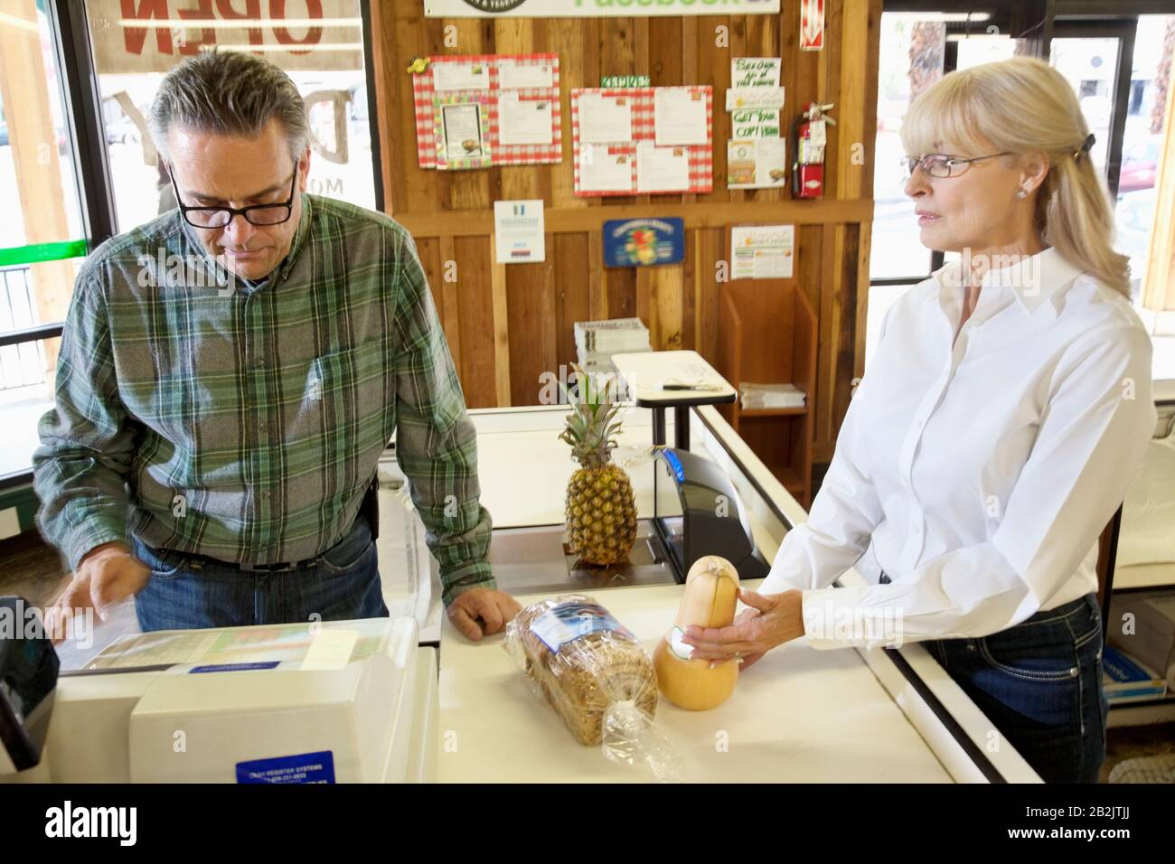 Mature owner with senior female customer at checkout counter in grocery ...