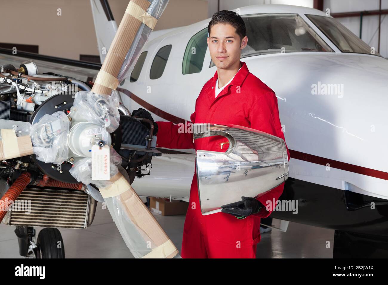 Portrait of young aeronautic engineer standing in front of an airplane ...