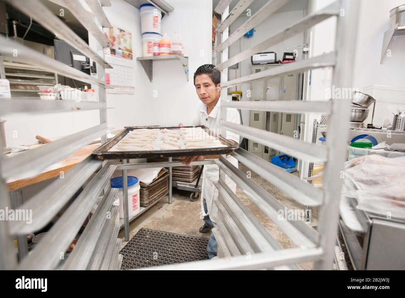 Young male baker placing bread tray on cart in commercial kitchen Stock ...
