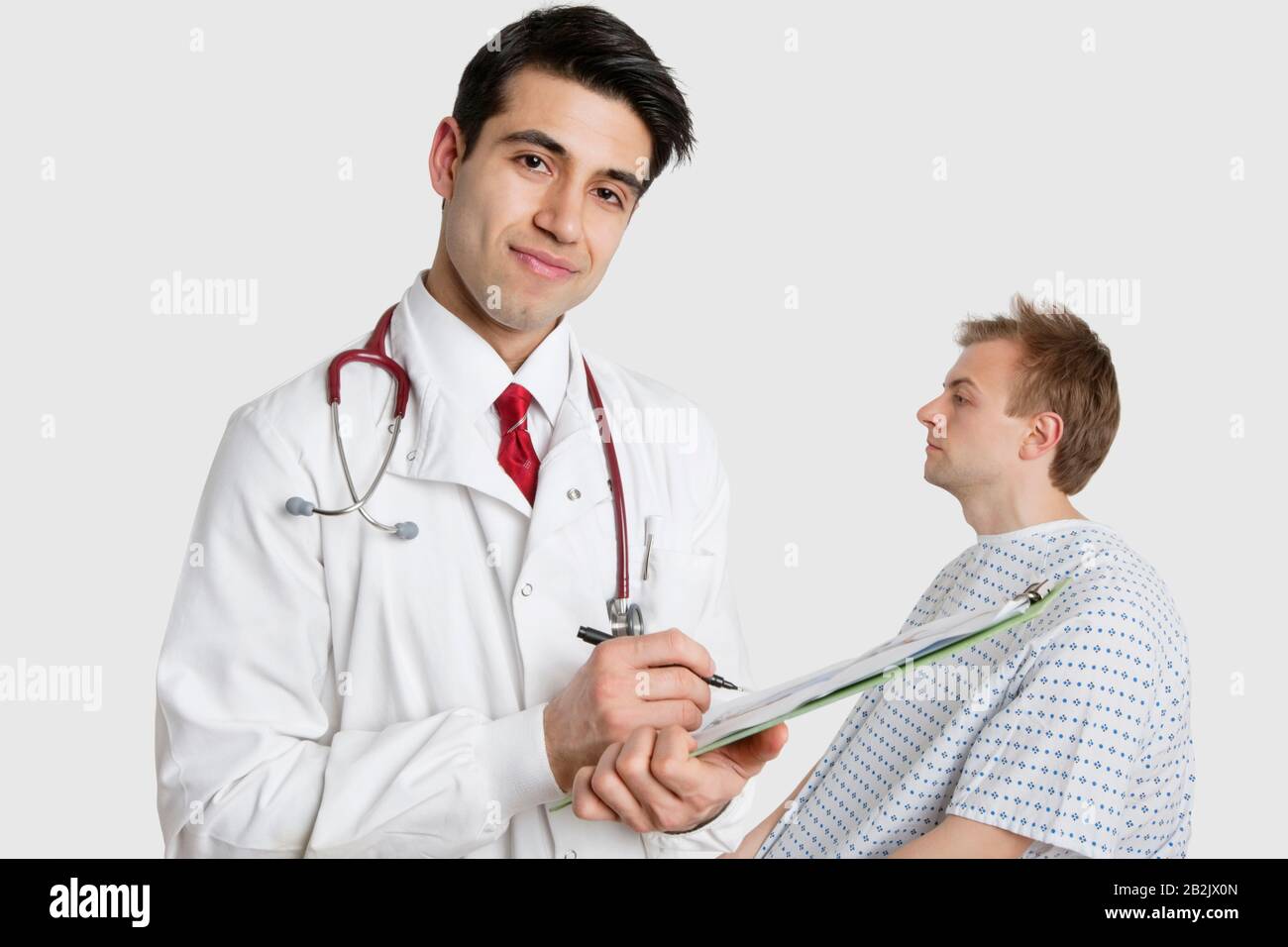Portrait of an Indian doctor writing prescription with patient sitting ...