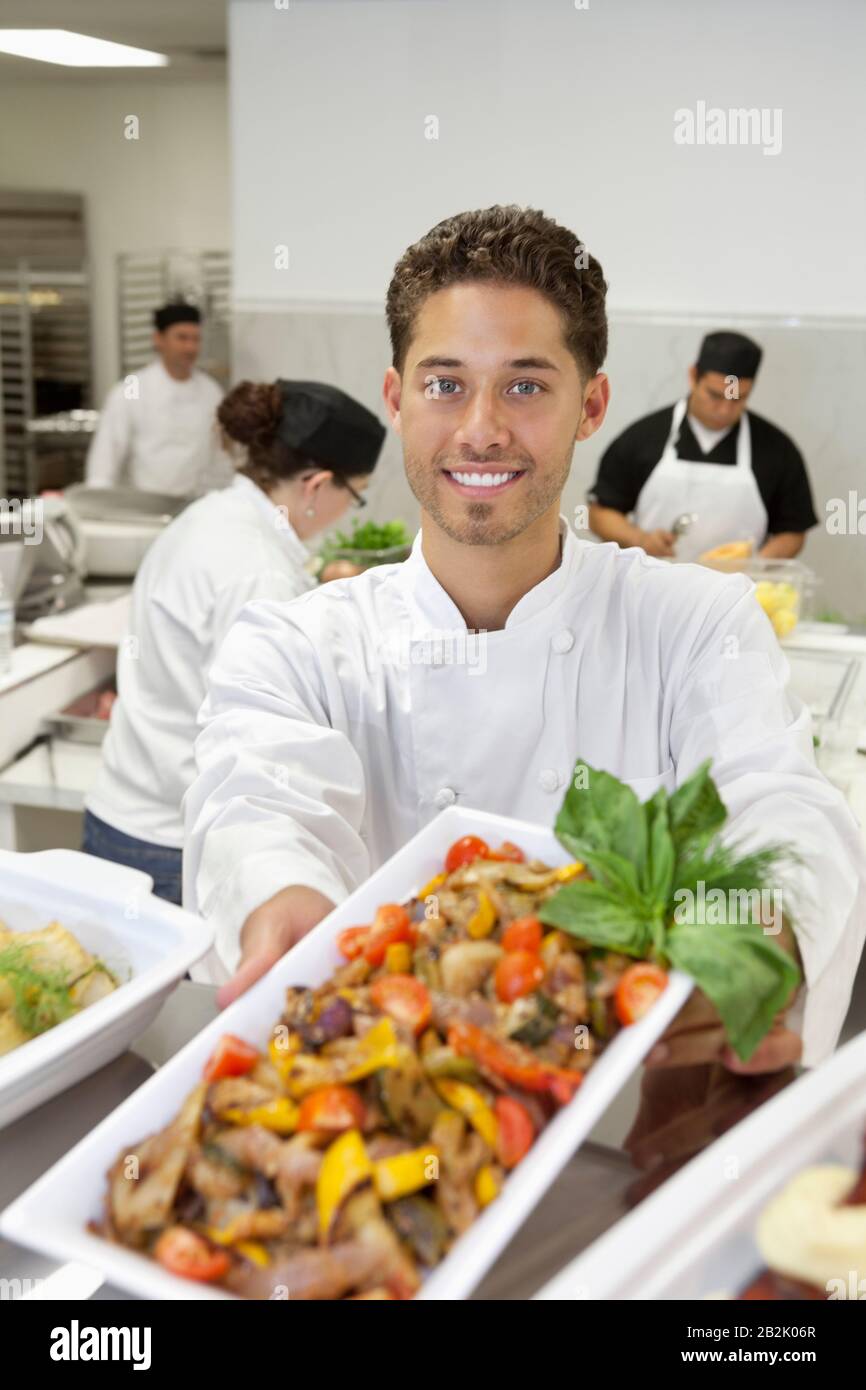 Portrait of male chef holding salad with coworkers in background Stock ...