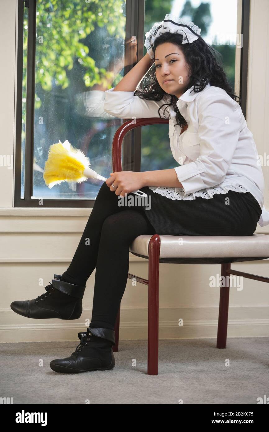 Pensive housemaid sitting on chair with a feather duster Stock Photo ...