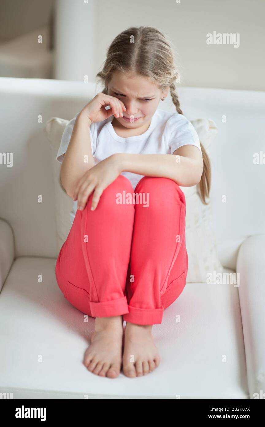 Young girl crying while sitting on sofa Stock Photo - Alamy