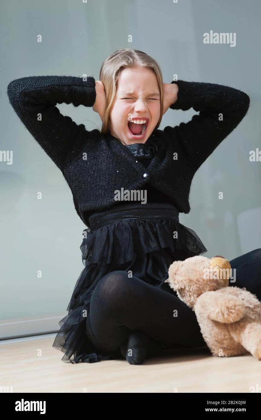 Frustrated young girl covering ears and screaming while sitting on ...