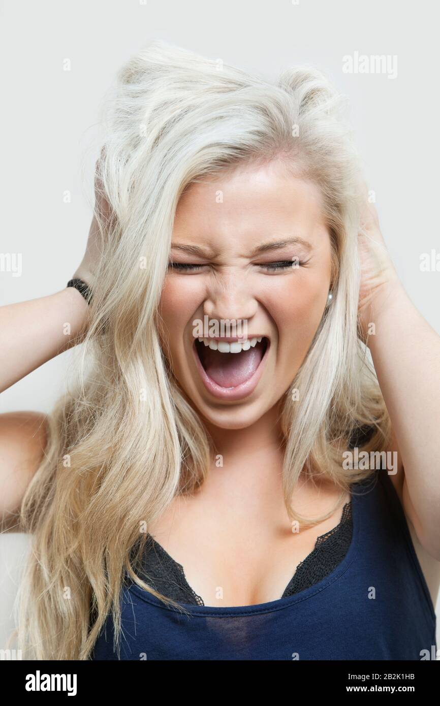 Frustrated woman with hands in hair over gray background Stock Photo ...