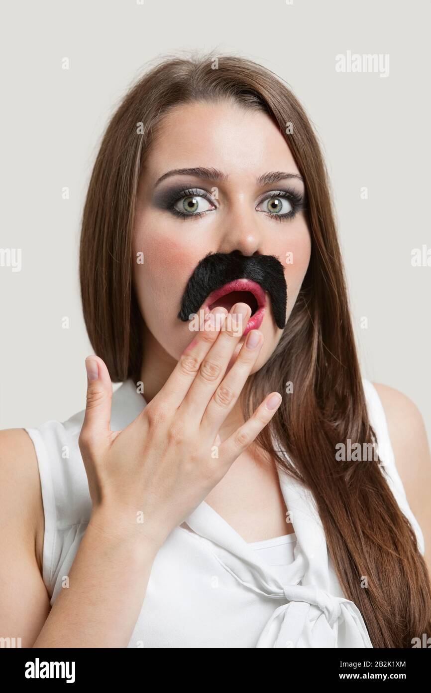 Portrait of shocked young woman with fake moustache over gray ...
