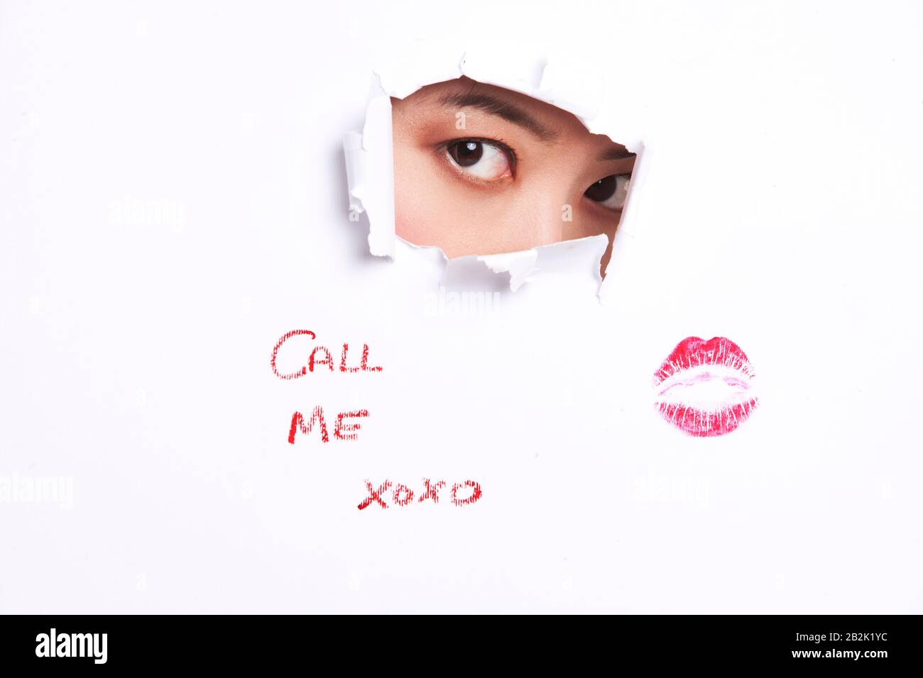 Young woman peeking through ripped paper with text message and lipstick ...
