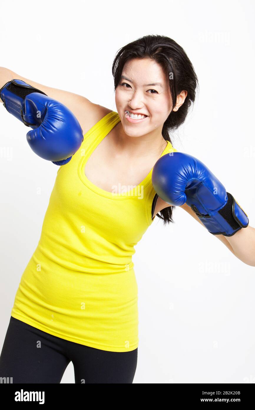 Portrait of happy Asian female boxer wearing blue gloves against white ...