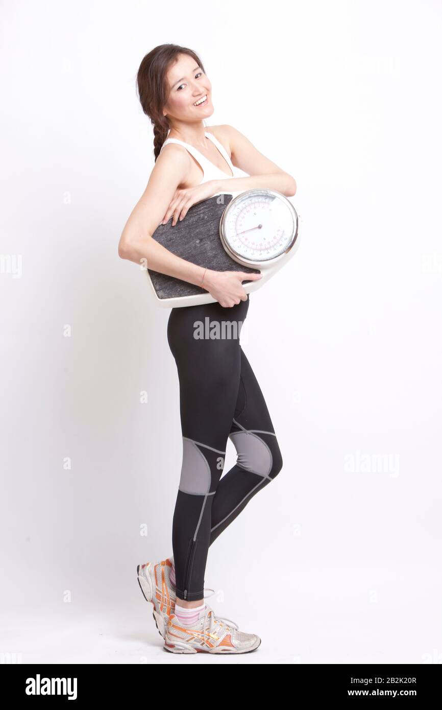 Portrait of young Asian woman with weight scale against white ...