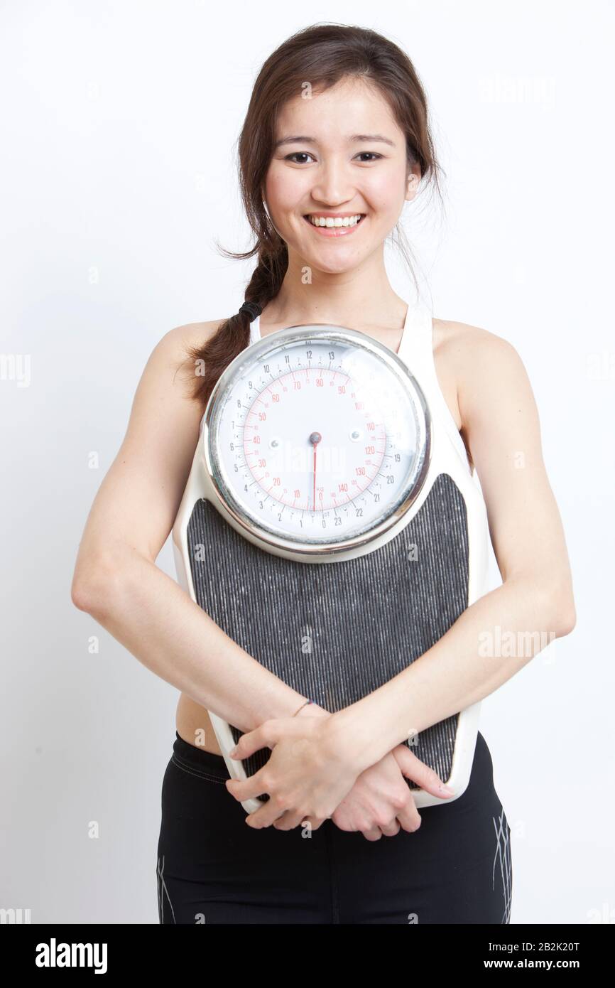Portrait of cheerful Asian woman holding weight scale against white ...