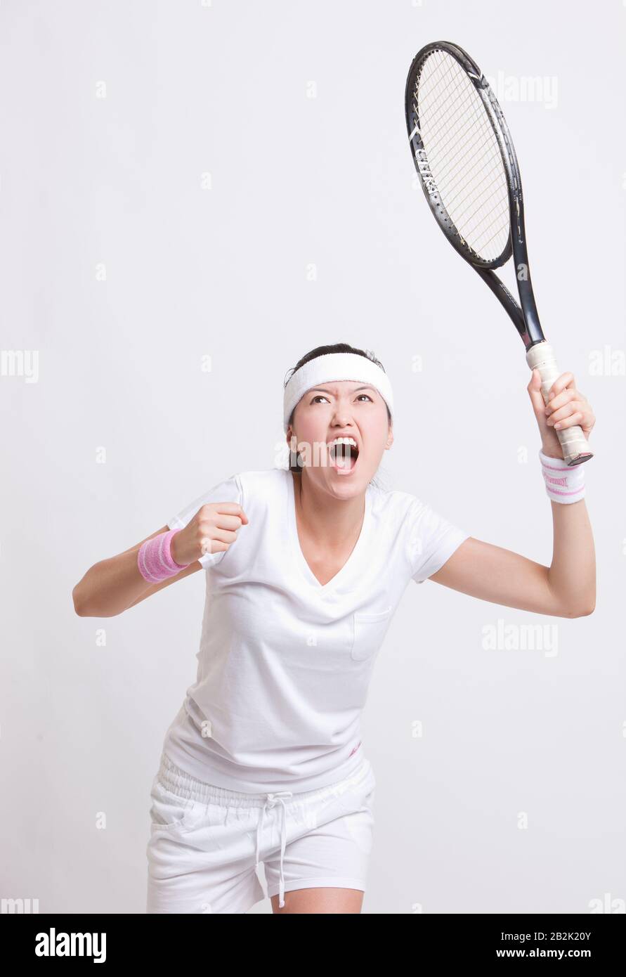 Young female tennis player with racket cheering against white ...