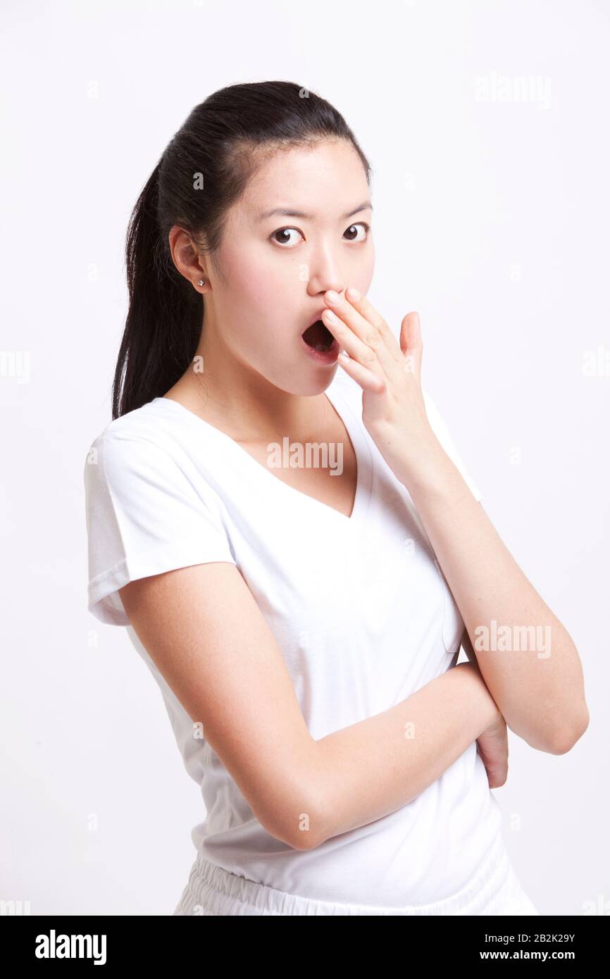 Portrait of shocked young woman with hand over mouth against white ...