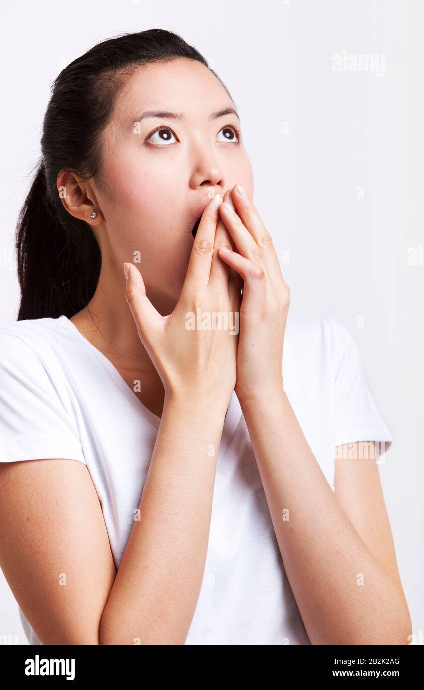 Shocked young woman with hands over mouth against white background ...