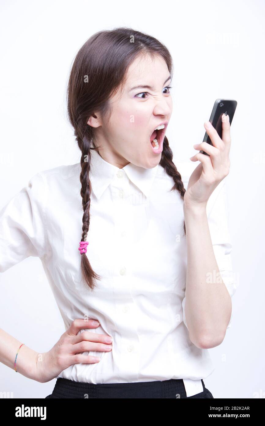 Furious young woman screaming into her cell phone against white ...