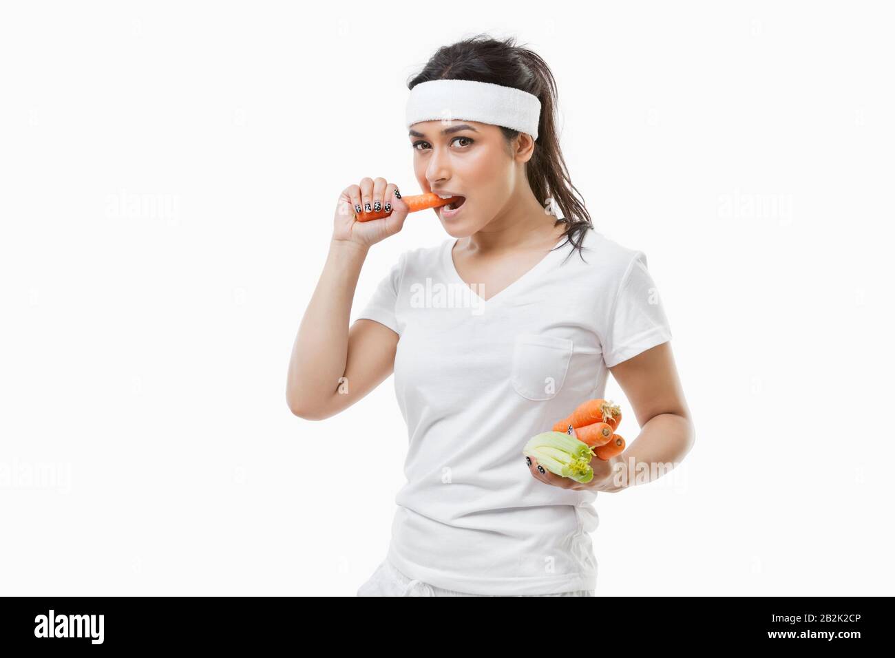 Portrait of young sportswoman eating carrot over white background Stock ...
