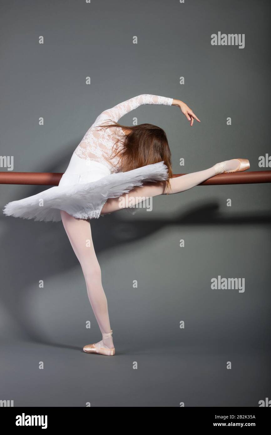 Young female ballet dancer stretching at ballet bar over grey ...