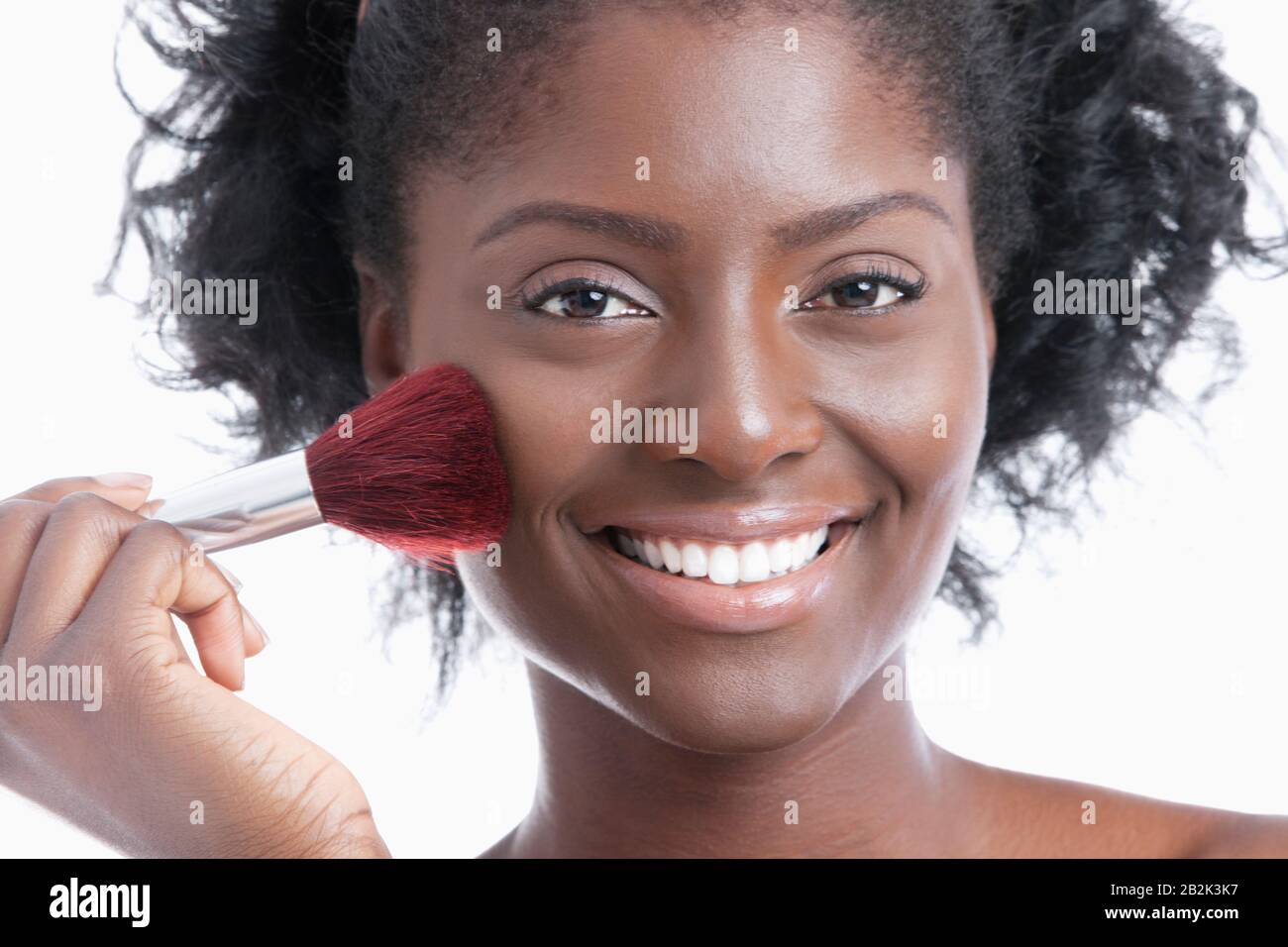 Portrait of a happy young woman applying blush over white background ...