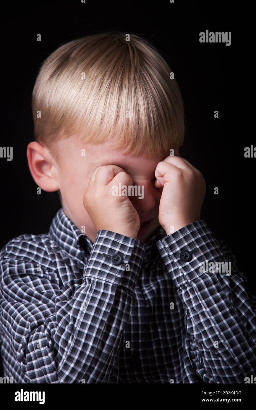 Young blonde boy crying in the studio with a black background Stock ...