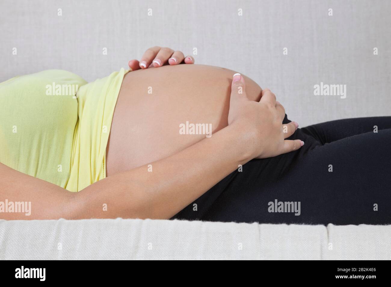 Midsection of young pregnant woman with hands on stomach relaxing at ...