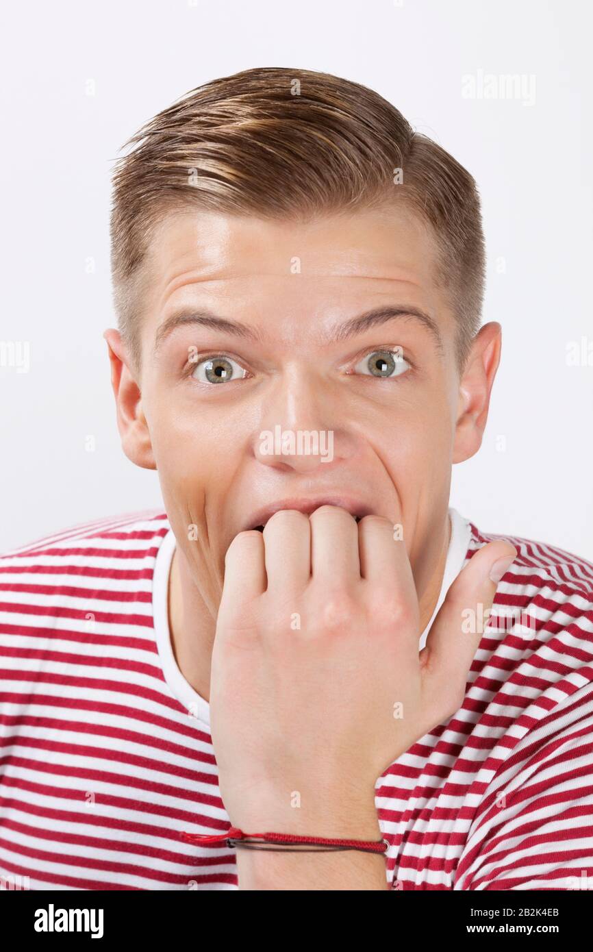 Portrait of amazed young man biting his finger over white background ...