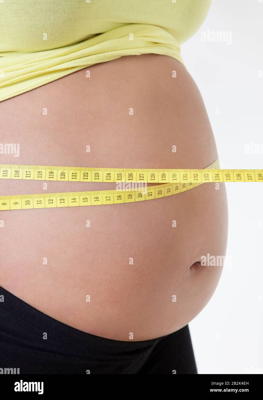 Midsection of pregnant woman measuring stomach with tape against white ...