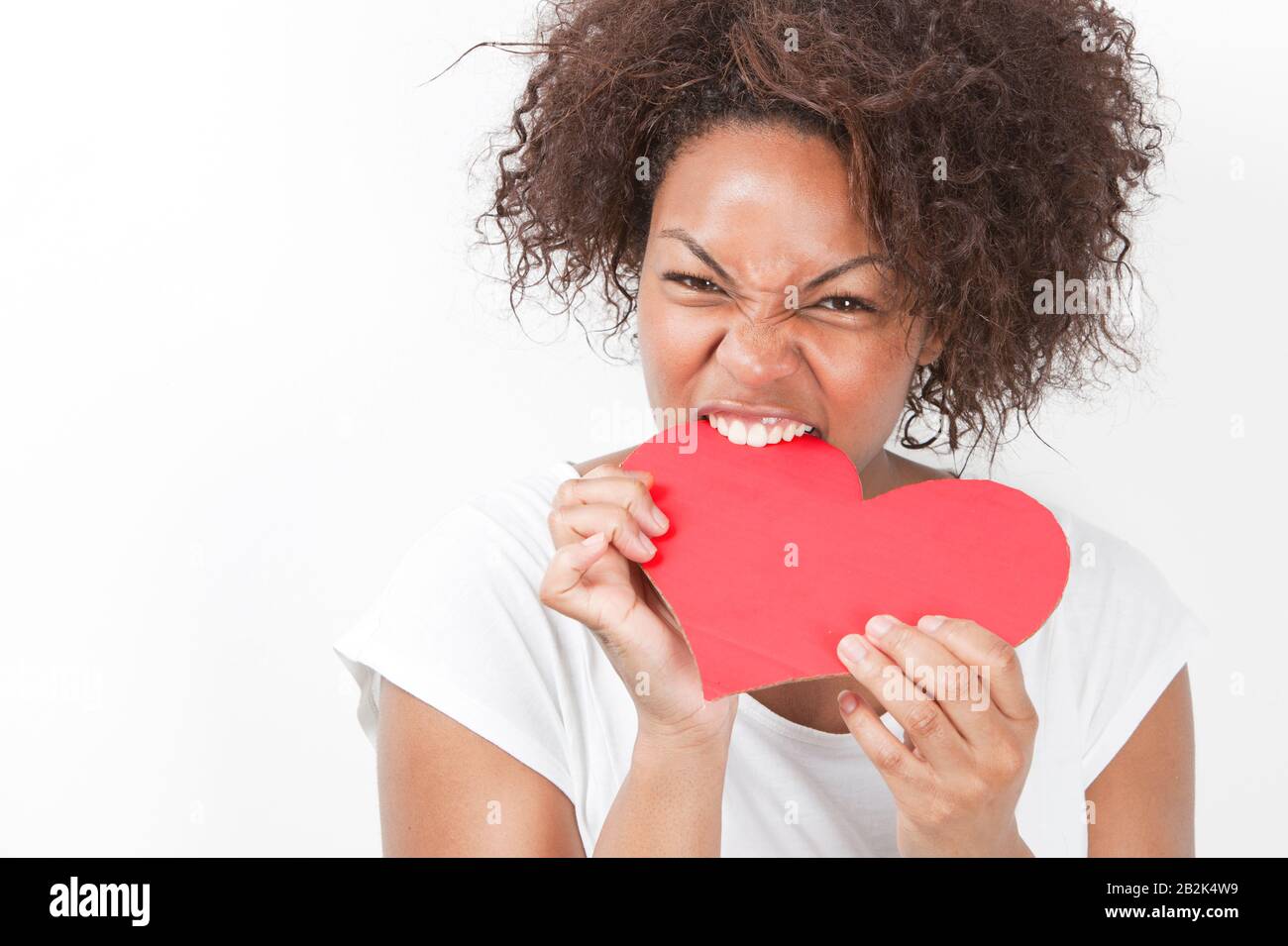 Portrait of frustrated young African American woman biting heart shape ...
