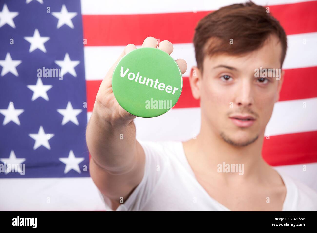 Portrait of young man displaying volunteer badge against American flag ...