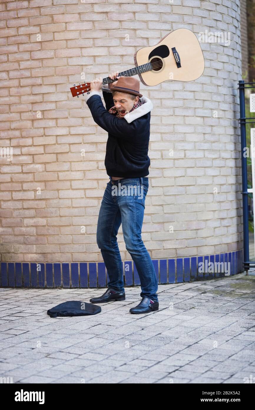 Aggressive young man breaking guitar against brick wall on street Stock ...