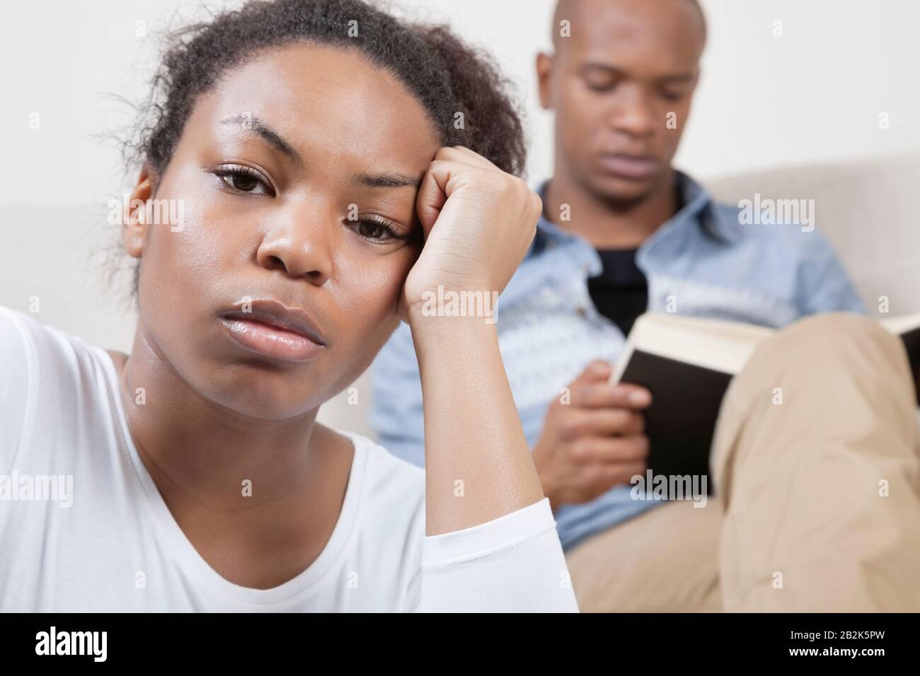 Portrait of sad young woman with man reading book in background Stock ...