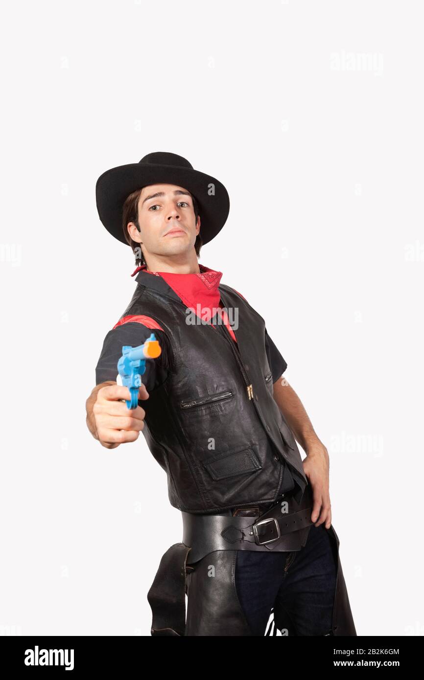 Portrait of young cowboy aiming handgun against gray background Stock ...